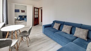 Uma sala de estar moderna com um sofá azul, uma mesa de jantar redonda e cadeiras cinzentas.