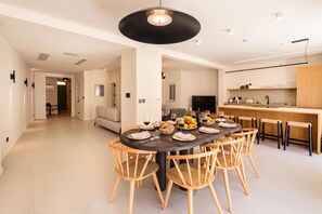 Uma zona de refeições moderna com uma mesa redonda posta para seis pessoas, rodeada por cadeiras de madeira.