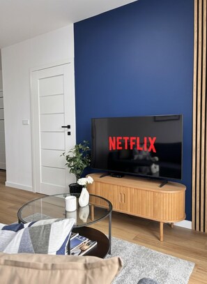 Uma sala de estar moderna com televisão de tela plana, um armário de madeira, uma mesa de centro de vidro e um vaso com planta.