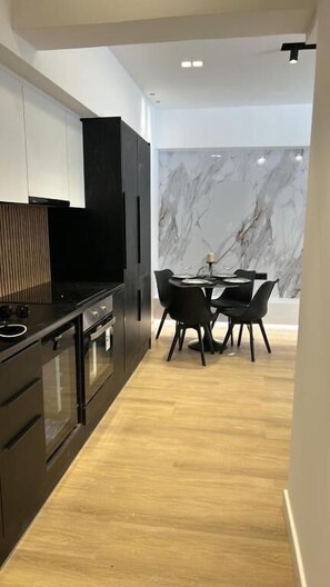 Uma cozinha moderna com armários escuros, uma área de jantar com parede de mármore e piso de madeira.
