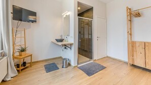 Quarto moderno com televisão de tela plana, uma cadeira de madeira, pia pequena e box de vidro.