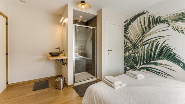 Quarto com cama, chuveiro e um grande mural de palmeira.