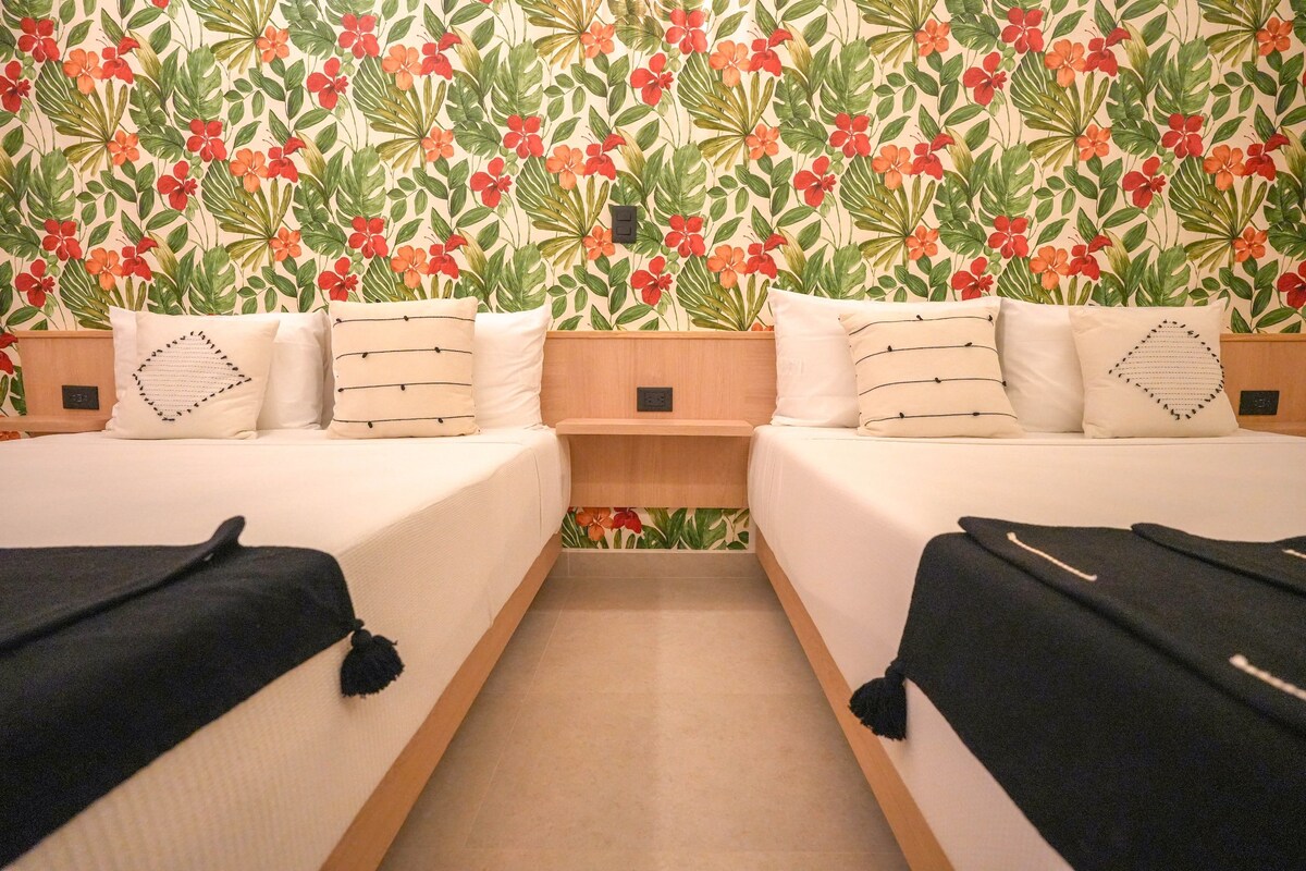 Quarto de casal com papel de parede floral, duas mesas de cabeceira e uma pequena prateleira de madeira.