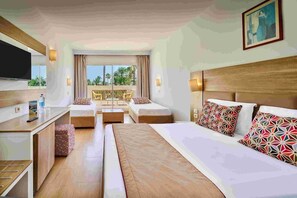 Quarto de hotel com cama, escrivaninha, televisão, varanda e vista para palmeiras, além de um quadro na parede.