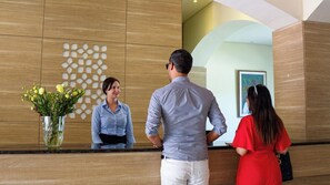 Balcão de recepção com um recepcionista, um homem e uma mulher atrás.