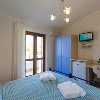 Quarto de hotel com cama, televisão, escrivaninha e guarda-roupa.
