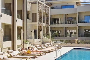 Área da piscina com espreguiçadeiras, piscina límpida e um edifício com varandas.