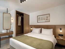 Quarto de hotel com cama, mesas de cabeceira, espelho, guarda-roupa e um quadro na parede.