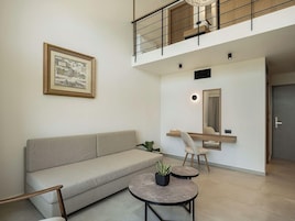 Uma sala de estar moderna com sofá, duas mesas redondas, um quadro emoldurado, um espelho e uma escada.