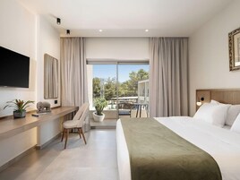 Quarto de hotel moderno com uma cama grande, uma escrivaninha, uma cadeira, uma televisão e uma varanda com vista.