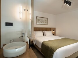 Quarto de hotel com uma pia grande e redonda, cama com manta verde, cabeceira de madeira e um quadro na parede.