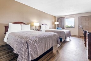 Quarto de hotel com duas camas, uma escrivaninha, uma cadeira, uma janela com cortinas e uma porta.