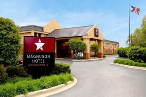 Entrada de hotel com placa, bandeira e céu claro.