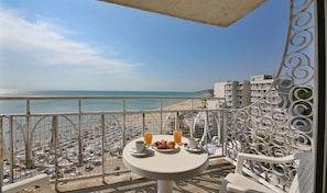 Varanda com mesa posta para dois, vista para uma praia com muitos guarda-sóis e céu limpo.