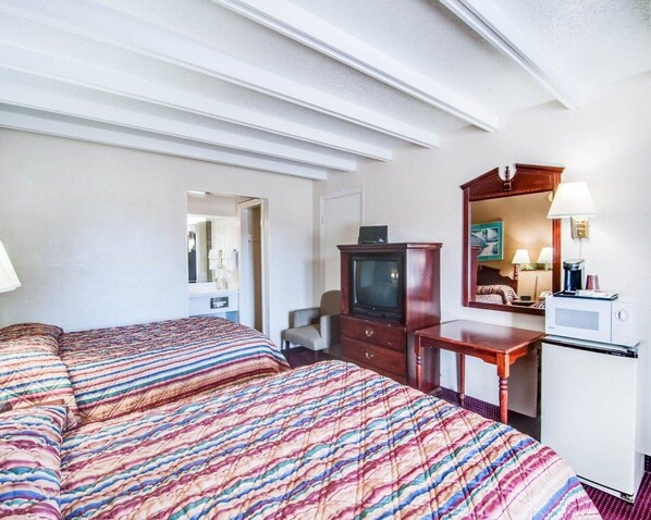 Quarto de hotel com duas camas, televisão, escrivaninha com abajur e micro-ondas.