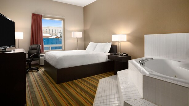 Quarto de hotel com cama, escrivaninha, televisão e banheiro com banheira.