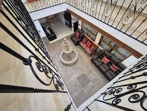 Um lobby espaçoso com uma fonte central, uma escadaria com corrimãos decorados e uma área de estar com um sofá e almofadas.