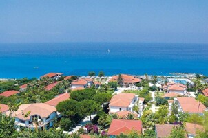 Zona residencial costeira com casas, piscina e vista clara para o mar.