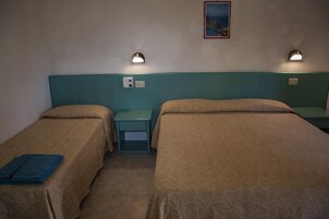 Quarto com duas camas de solteiro, cada uma com cabeceira e peseira, uma pequena mesa de cabeceira e luminária fixada na parede.