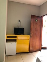 Quarto com escrivaninha amarela, televisão e mini-geladeira branca.