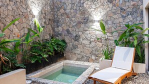 Muro de pedra, uma pequena piscina e uma espreguiçadeira em um jardim.