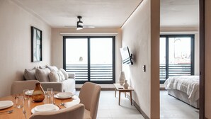 Quarto de hotel moderno com área de refeições, sofá, cama e janelas amplas.