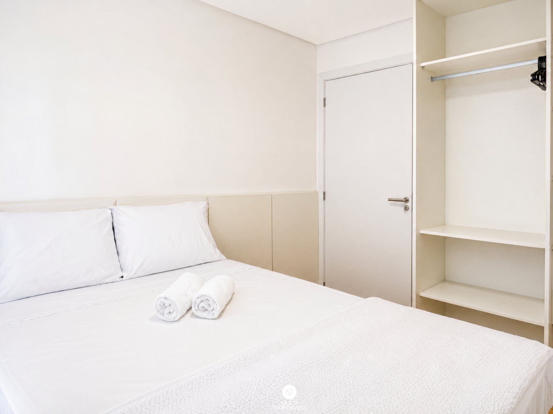 Quarto de hotel com cama, guarda-roupa e prateleira.