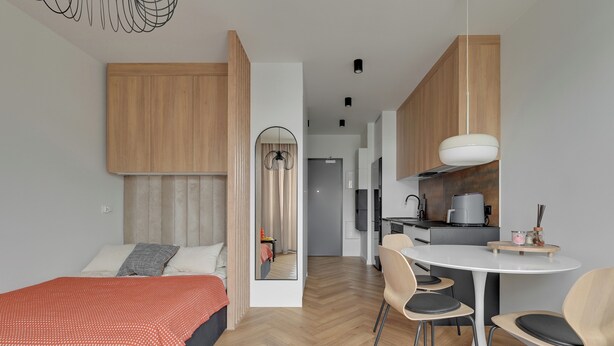 Quarto moderno com cama, uma mesinha, uma cadeira, cozinha compacta e um espelho.