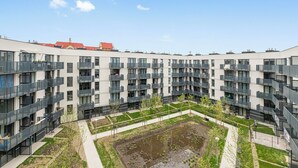 Um edifício de apartamentos moderno com várias varandas, um pátio com árvores jovens e um céu claro.