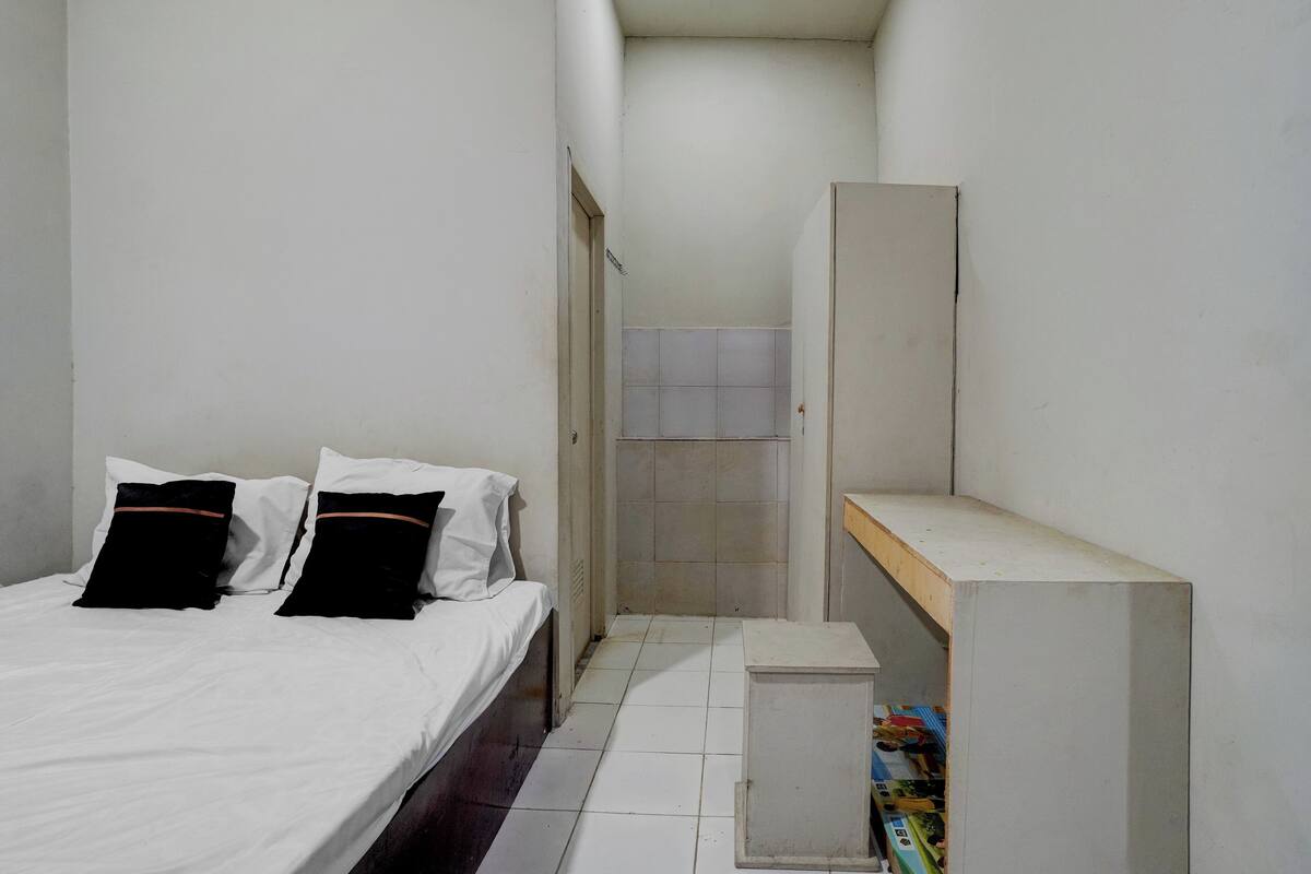 Quarto pequeno e estreito com uma cama de solteiro, um guarda-roupa branco e um pequeno armário.