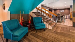 Um hall de hotel com cadeiras verde-água, uma escada e um balcão de recepção.