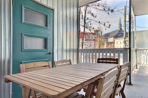 Mesa e cadeiras de madeira numa varanda com porta azul-turquesa e grades brancas.