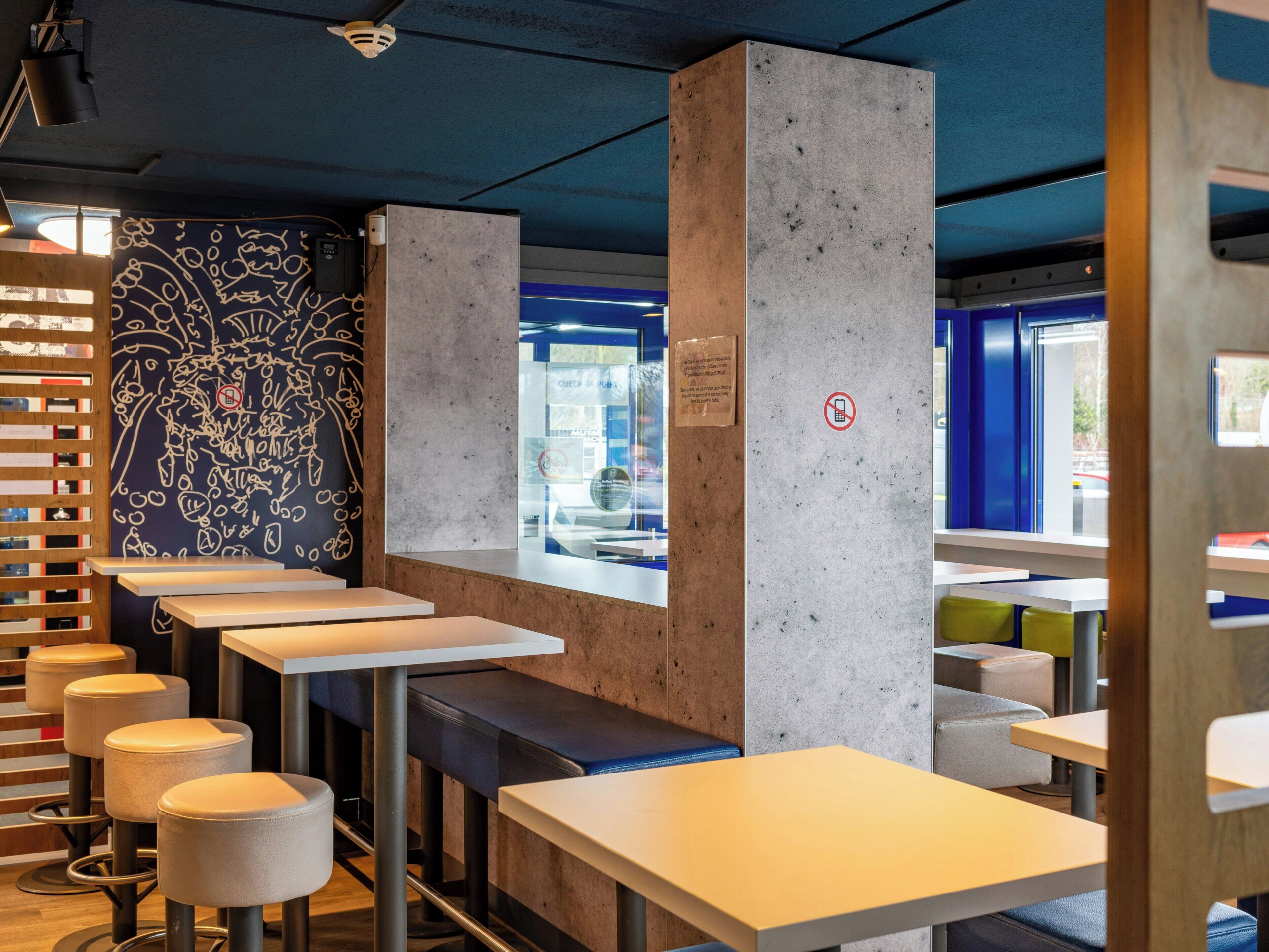 Um interior moderno com pilares de concreto, mesas e banquetas brancas.