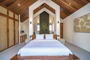 Uma cama grande em um quarto com vigas de madeira, parede de pedra e luminária moderna.