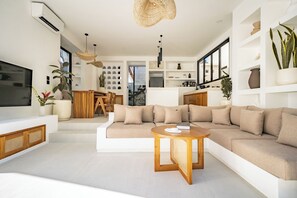 Uma sala de estar moderna com um sofá de canto, uma mesa de centro redonda de madeira e uma televisão.