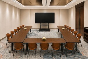 Uma sala de conferências com uma mesa comprida, cadeiras, uma TV de tela plana e piso carpeteado.