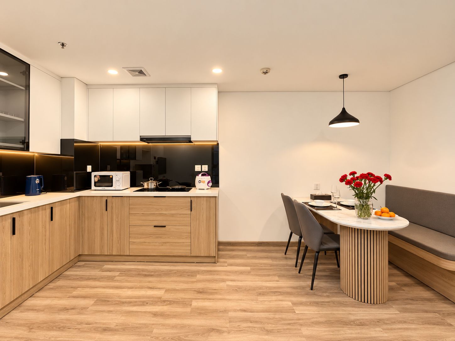 Cozinha moderna com armários de madeira, micro-ondas embutido e área de jantar com mesa redonda e cadeiras.