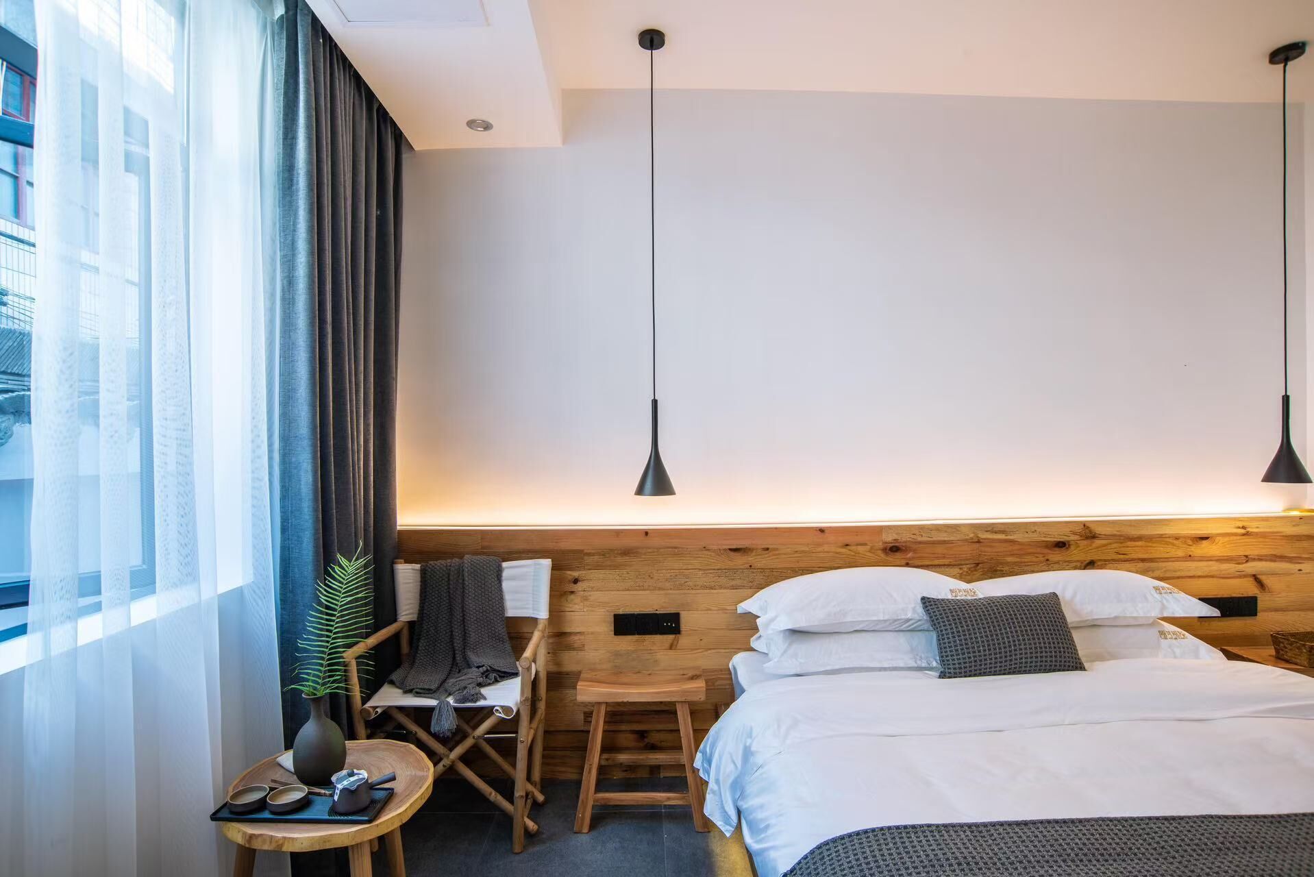 Quarto de hotel com cama, escrivaninha, cadeira e janela com cortinas.