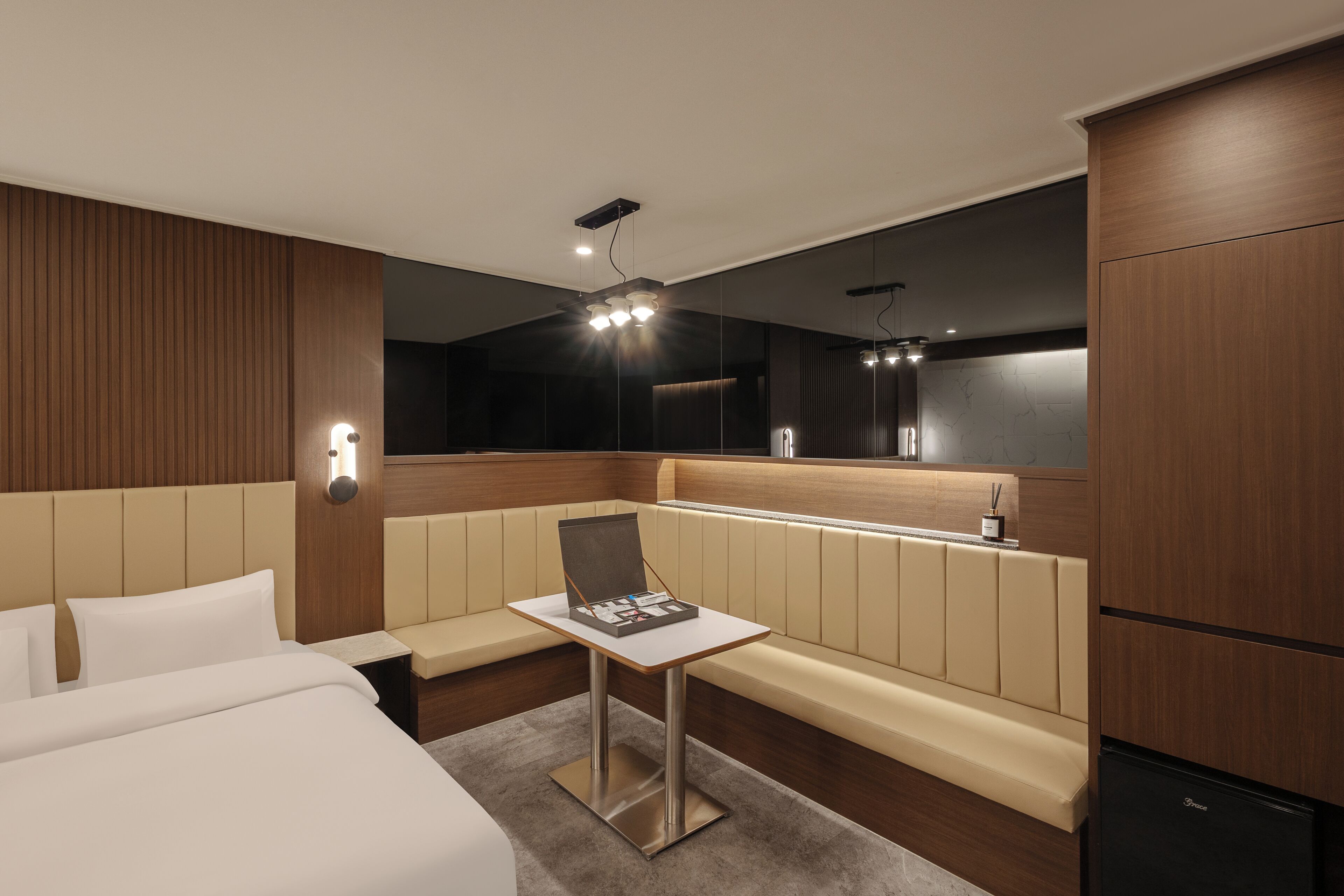 Quarto de hotel moderno com uma cama, uma mesinha com um laptop, um espaço de estar e um espelho grande.