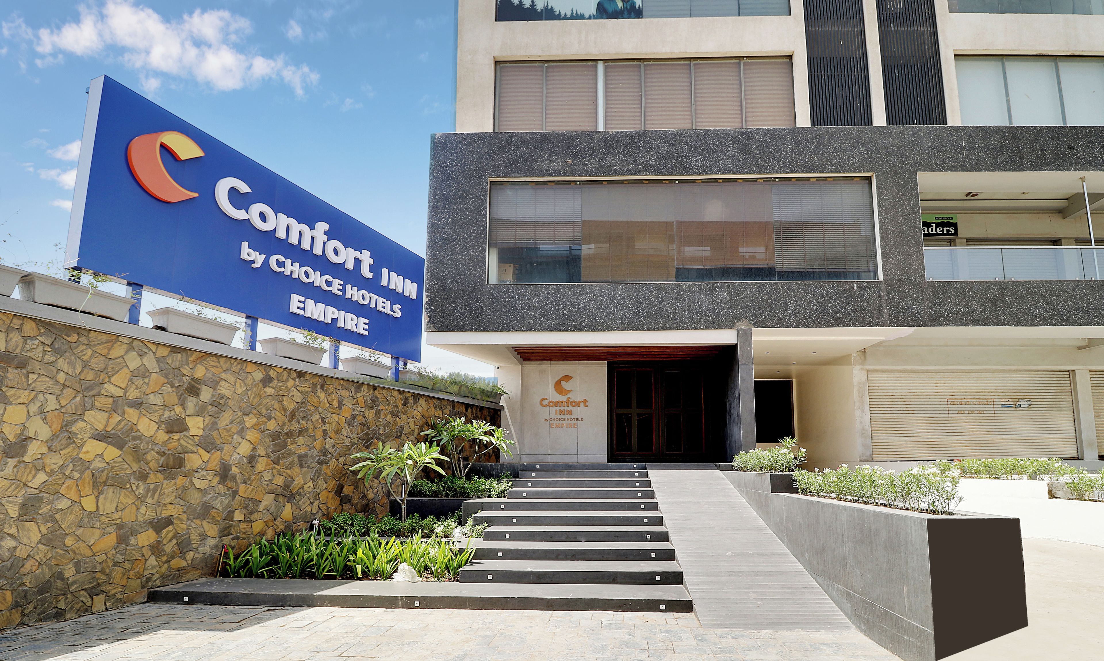 Entrada de um hotel com parede de pedra, degraus que levam à porta e uma grande placa azul indicando que é um Comfort Inn da Choice Hotels Empire.