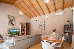 Uma sala de estar moderna com teto de madeira, televisão, sofá, mesa de jantar posta para dois e estante de livros.