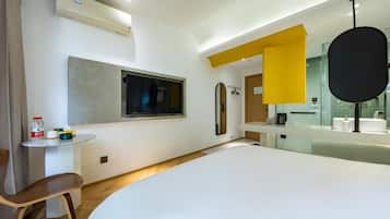 Quarto de hotel moderno com uma cama grande, uma mesinha redonda com uma cadeira, televisão, espelho e banheiro com pia e vaso sanitário.