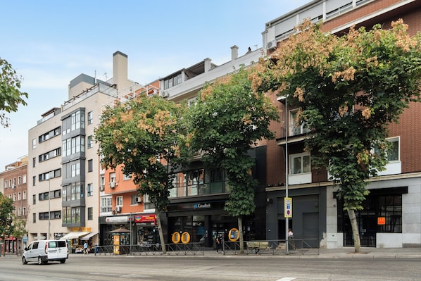 Um edifício de vários andares com fachada moderna, uma vitrine visível com um letreiro e uma árvore na frente.