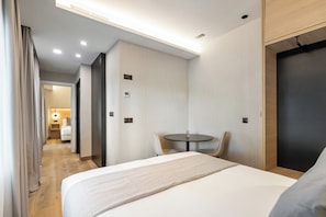 Quarto de hotel moderno com uma cama grande, uma mesa redonda e uma área de estar separada.