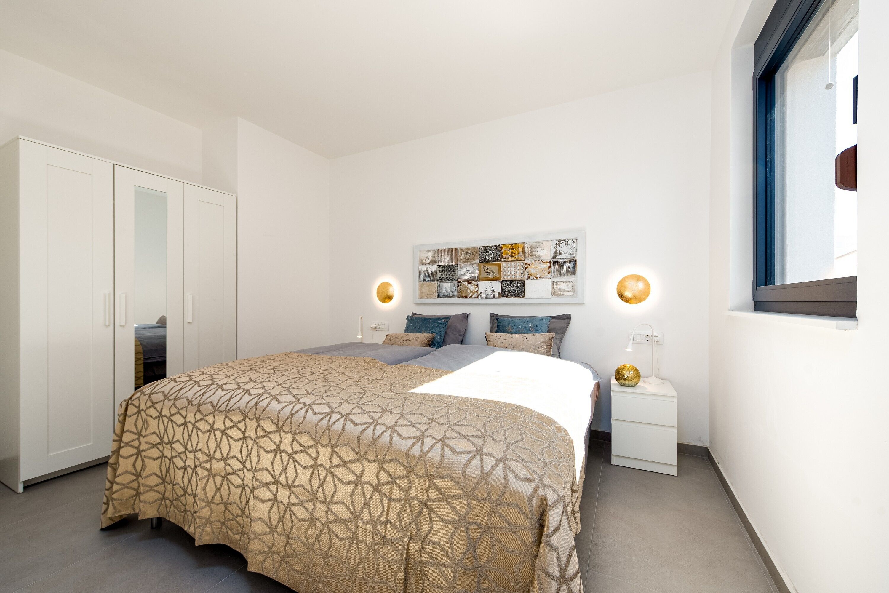 Um quarto com cama, mesas de cabeceira, guarda-roupa e uma obra de arte na parede.