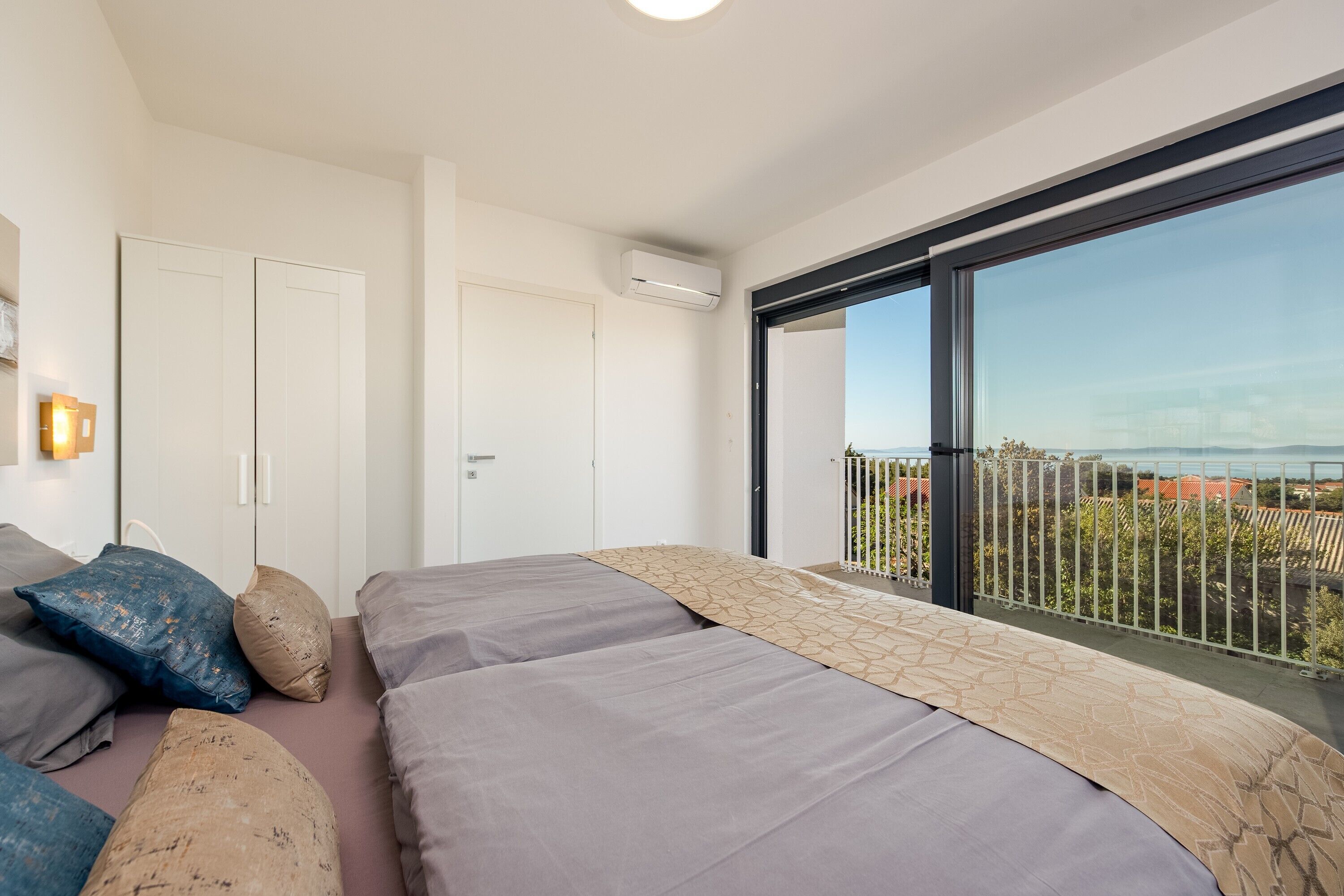 Quarto com uma janela ampla, cama com roupa de cama estampada e vista para o exterior.