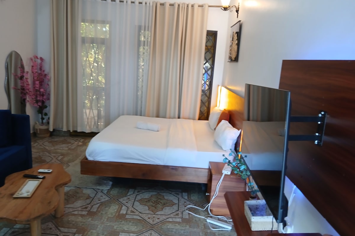 Quarto de hotel com cama, escrivaninha, cadeira, televisão e janela com cortinas.