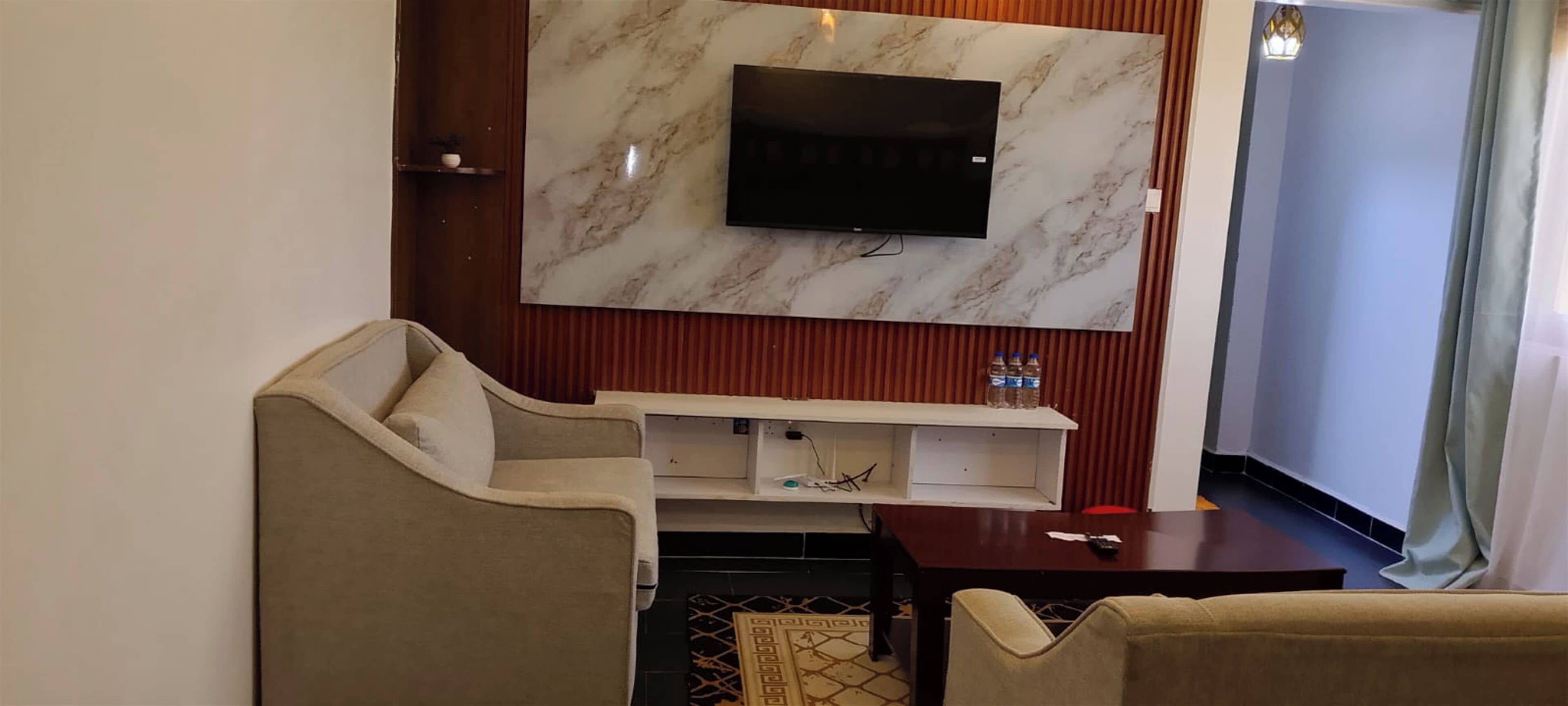 Uma sala de estar com televisão de tela plana presa a uma parede de mármore, um sofá, uma mesa de centro e uma pequena mesa lateral.