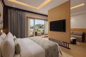 Quarto de hotel com uma cama grande, TV de tela plana, varanda com vista e um sofá.