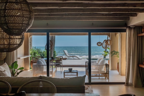 Quarto com vista para o mar, mobiliado com cadeiras de vime e um sofá, e um grande candeeiro de luz trançada.